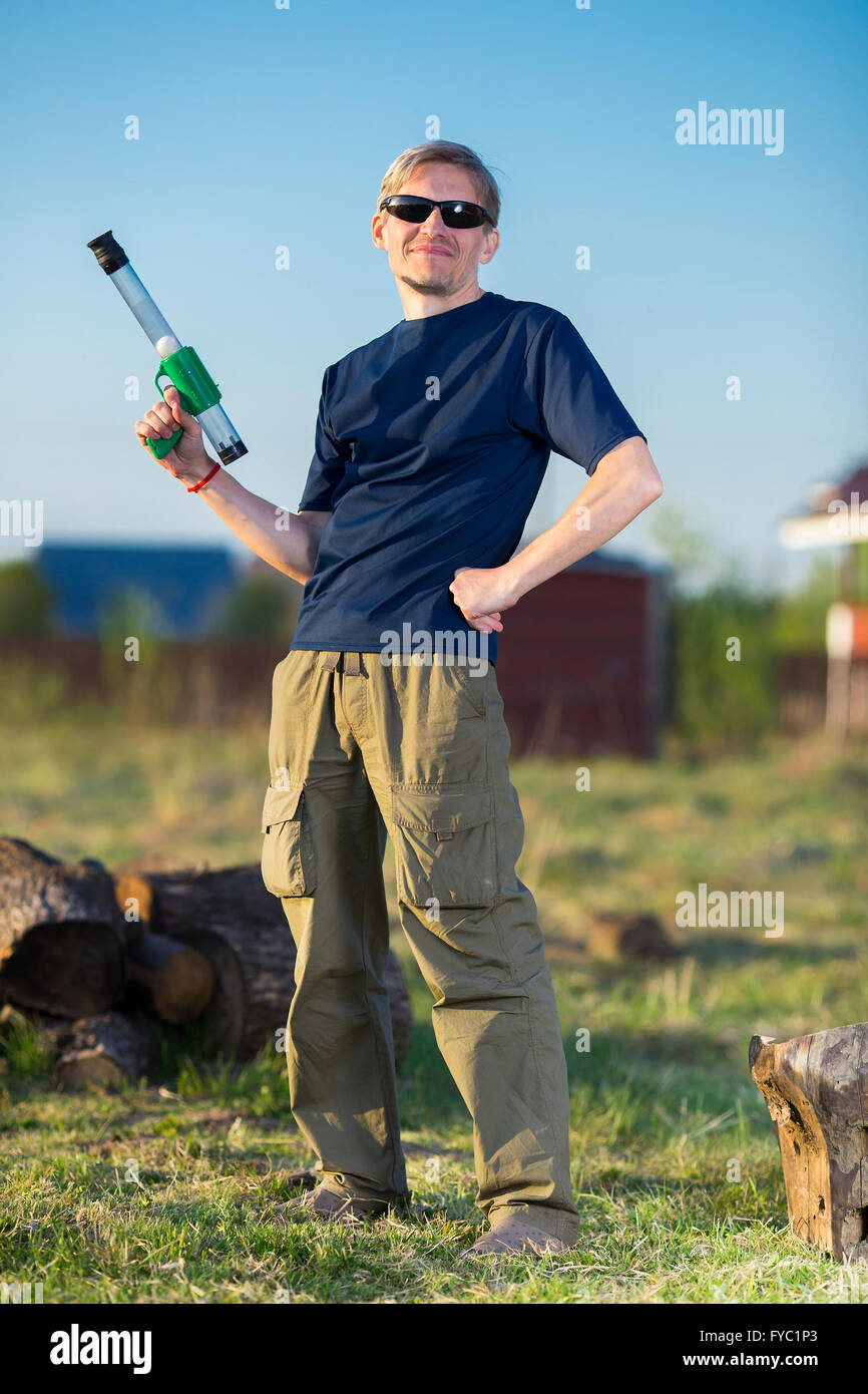 Tough man in sunglasses standing with toy gun on natural background ...