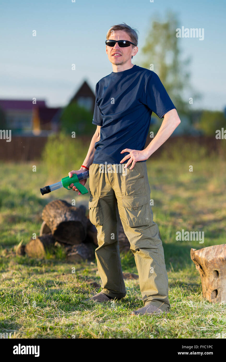 Tough man in sunglasses standing with toy gun on natural background ...