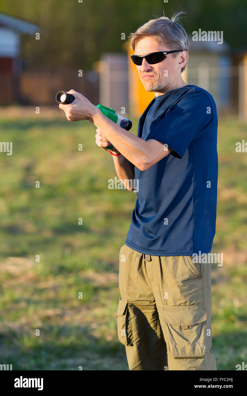 Tough man in sunglasses standing with toy gun on natural background ...