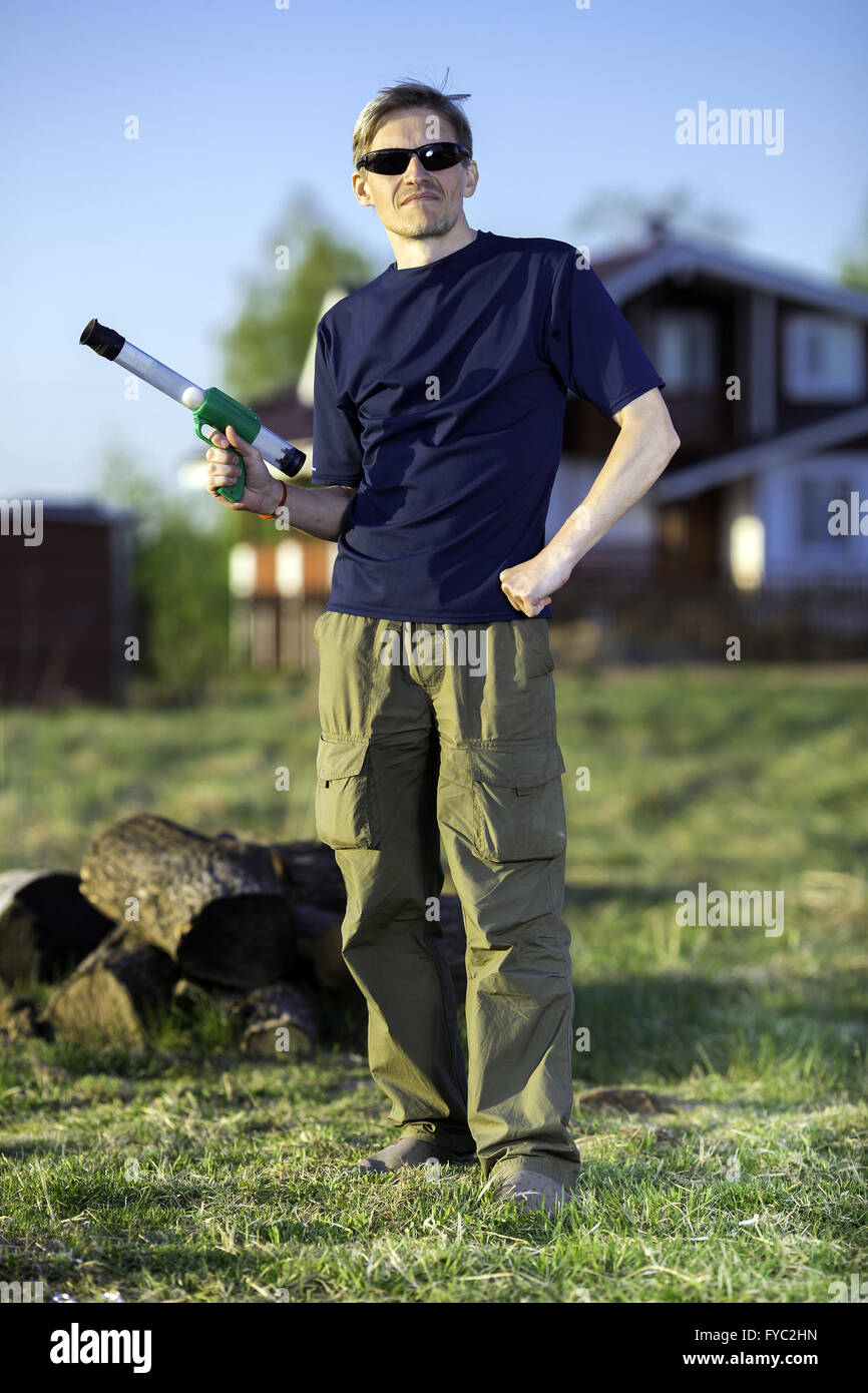 Tough man in sunglasses standing with toy gun on natural background ...