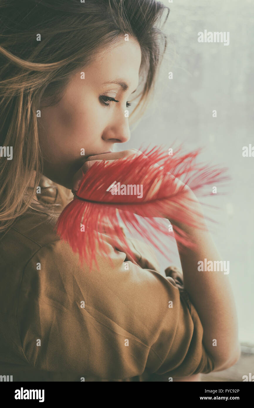 Beautiful young woman holding a red feather by the window Stock Photo ...
