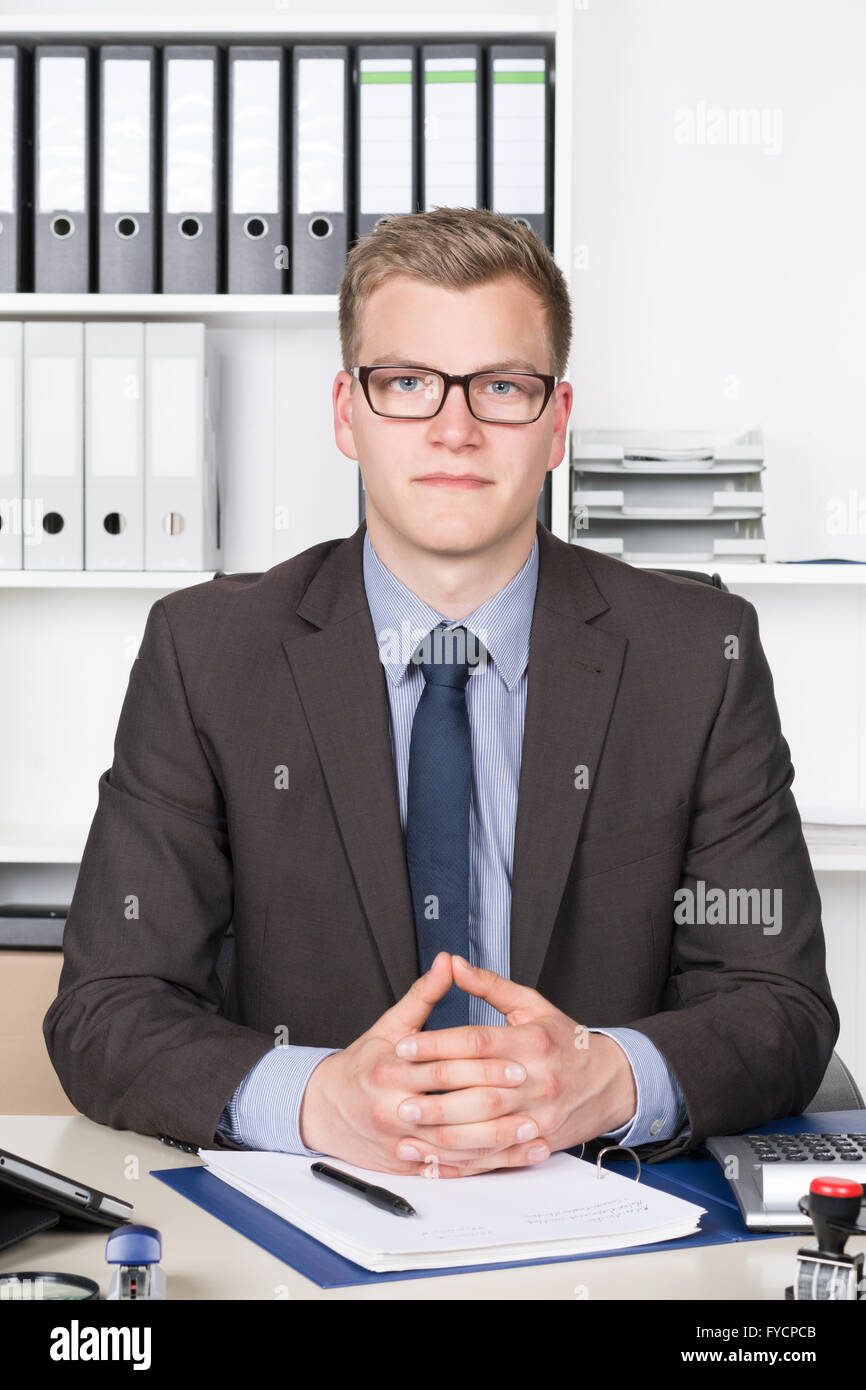 Young businessman is sitting with folded hands at the desk in the ...