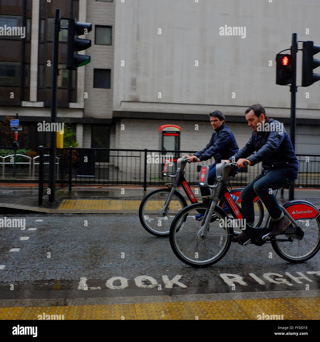 two men riding Boris Bikes in the rain over "Look Right" marking on ...
