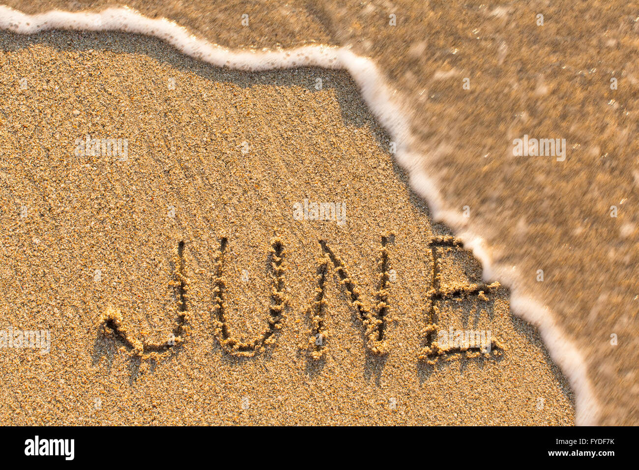 June - word drawn on the sand beach with the soft wave. Months series ...