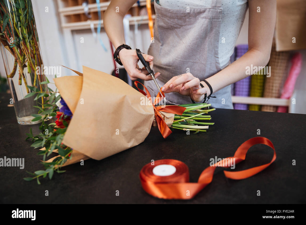 Closeup of hands of young woman florist making bow with red ribbon on ...
