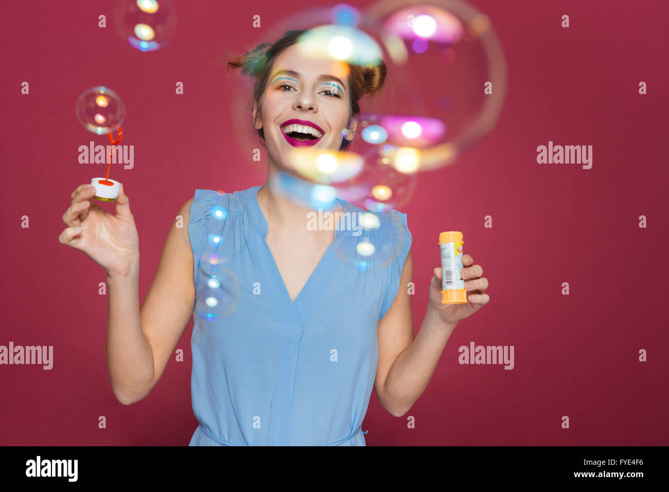 Happy charming young woman smiling and blowing bubbles over pink ...