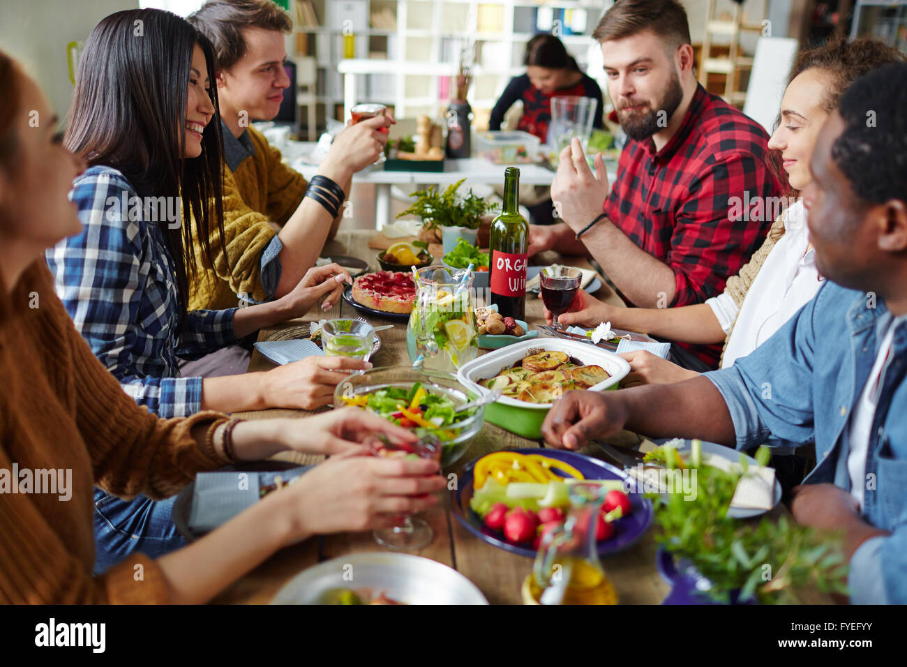 Group of happy friends sitting by table and having dinner Stock Photo ...