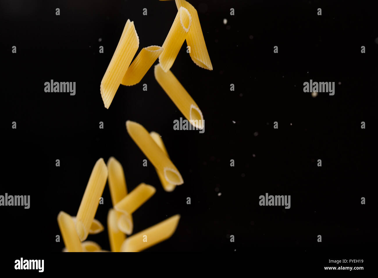 Falling penne pasta. Flying yellow raw macaroni over black background ...
