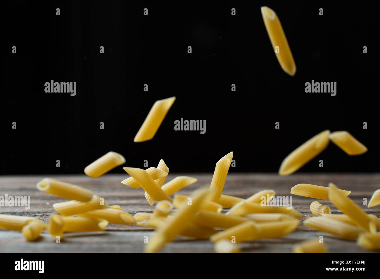 Falling penne pasta. Flying yellow raw macaroni over black background ...
