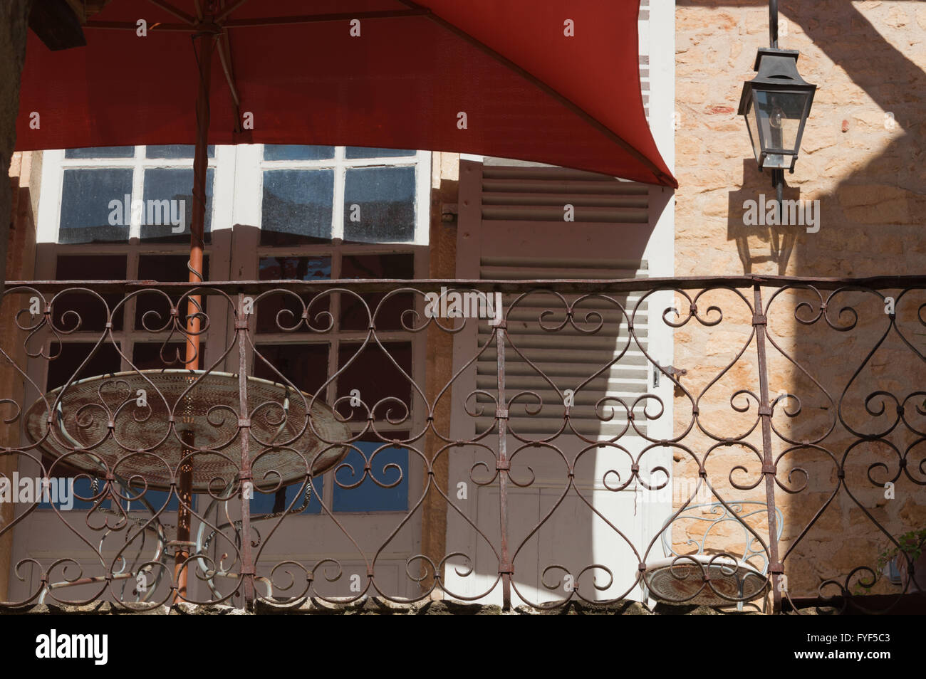 Red parasol and rusting metal table and chair on a balcony of french ...