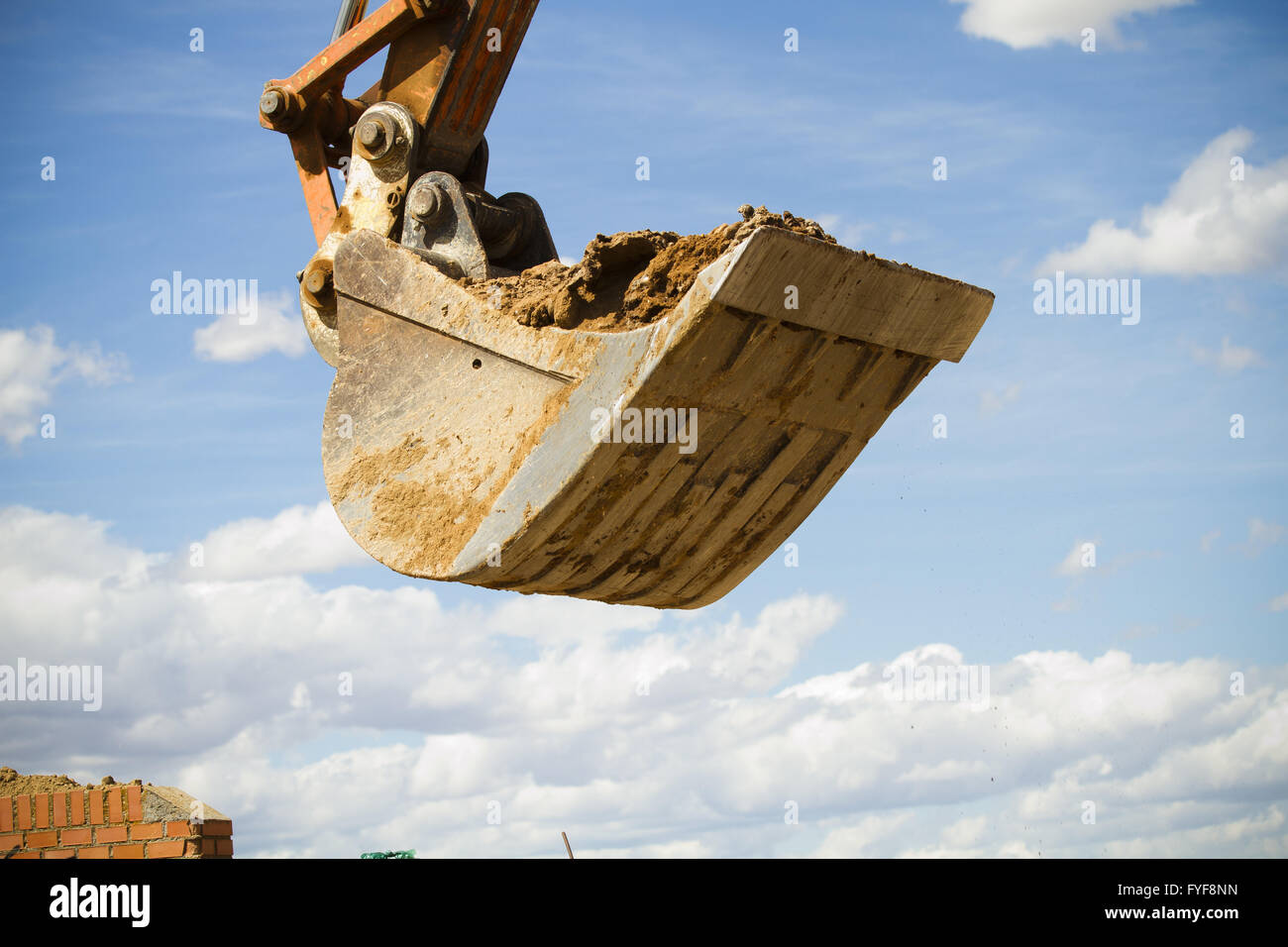 Excavator standing in sandpit with raised bucket over cloudscape sky ...