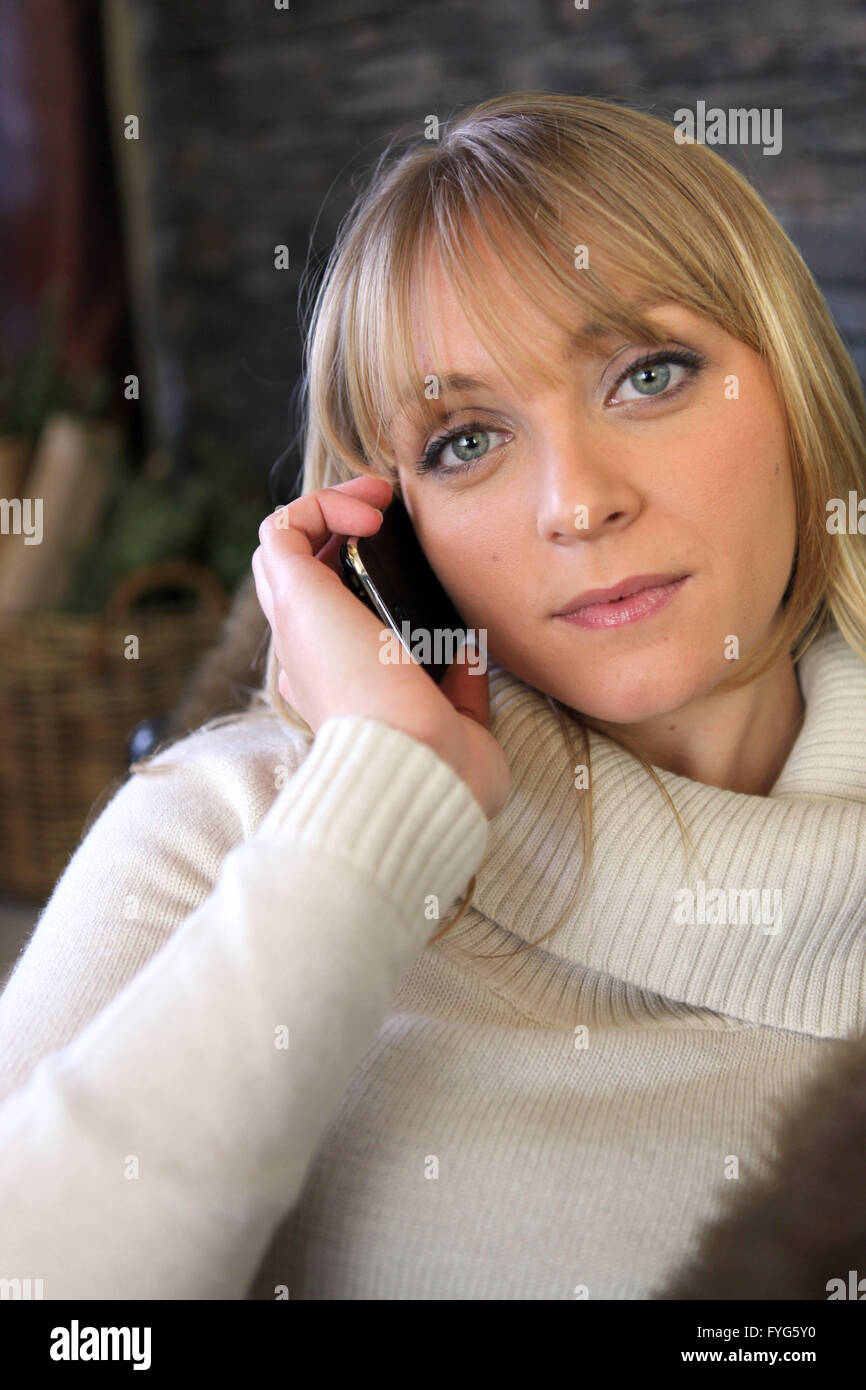 Blond woman making phone call whilst sat on cosy sofa Stock Photo - Alamy