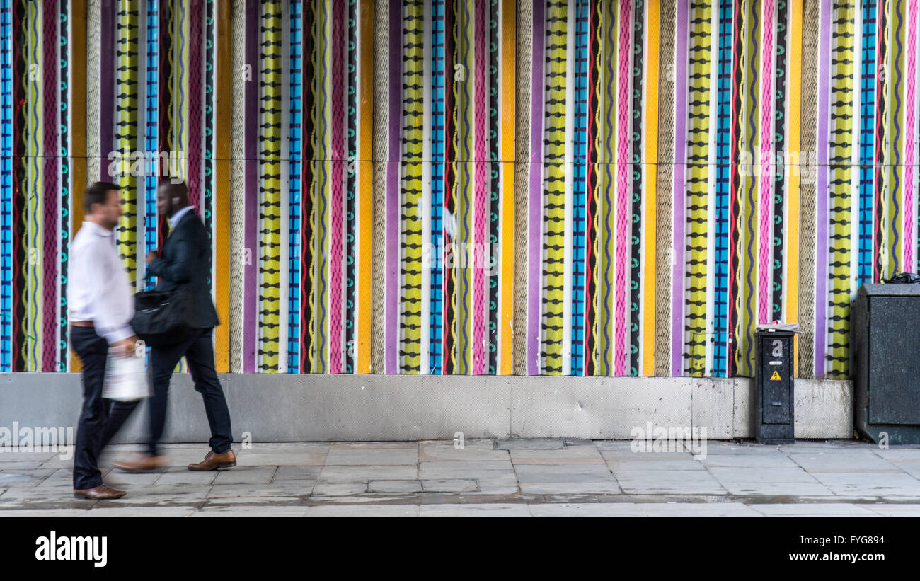 A pair of unidentifiable businessmen pass a colourful stripe mural on ...