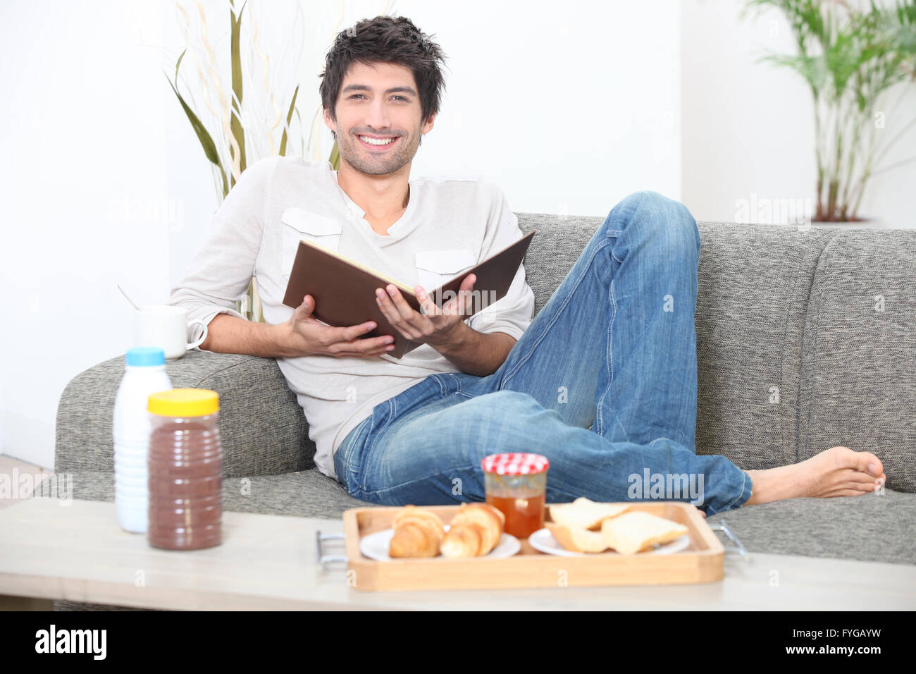 Man sitting on a sofa eating breakfast and reading a book Stock Photo ...
