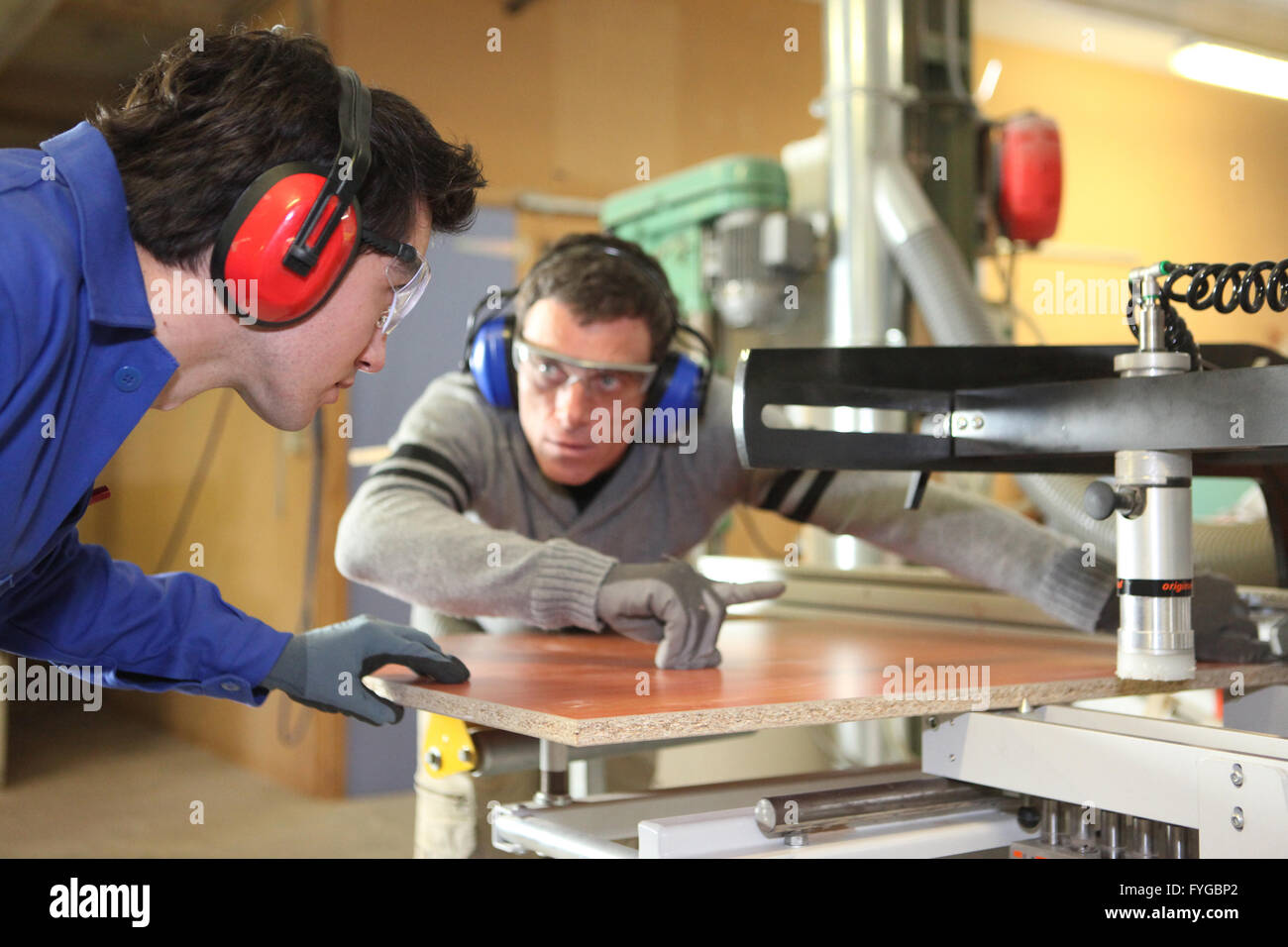 An experienced worker showing an apprentice how to cut a piece of wood ...