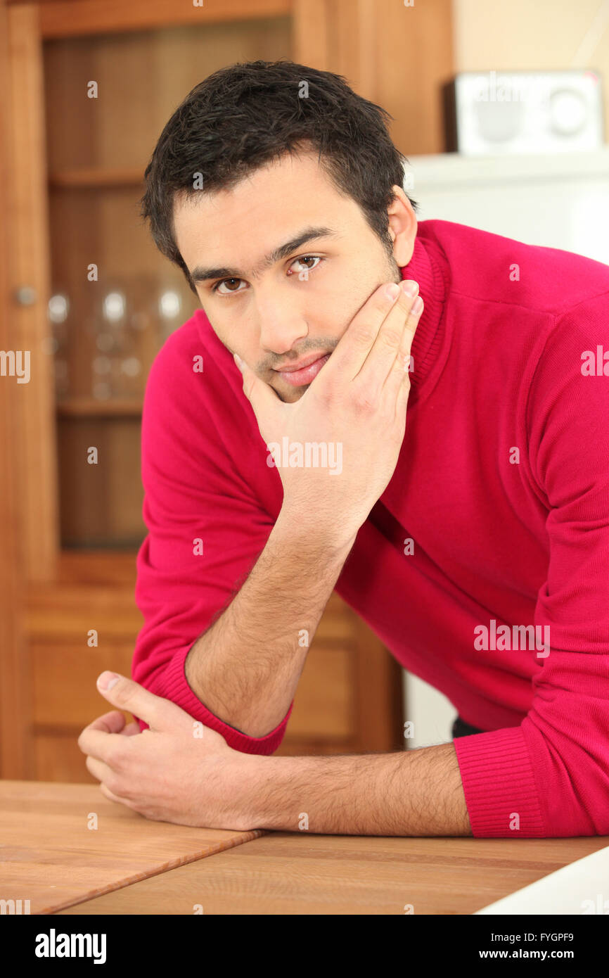 young dark-haired guy in kitchen wearing raspberry red jumper Stock ...