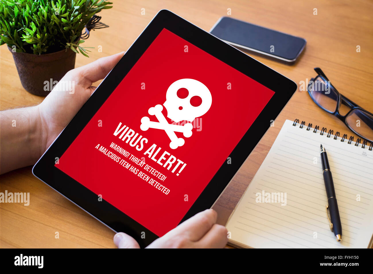 hands of a man holding a virus infected device over a wooden workspace ...