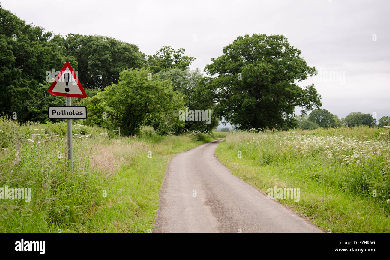 A sign beside a single track country lane road warning of potholes ...