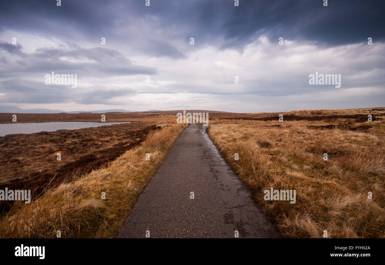 A road in a poor state of repair on wide empty peat bog moorland, The ...