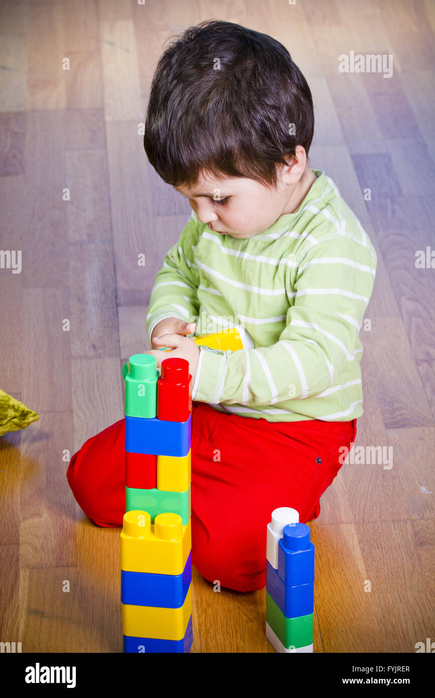 Brunette child playing with color tower toy in wooden room Stock Photo ...