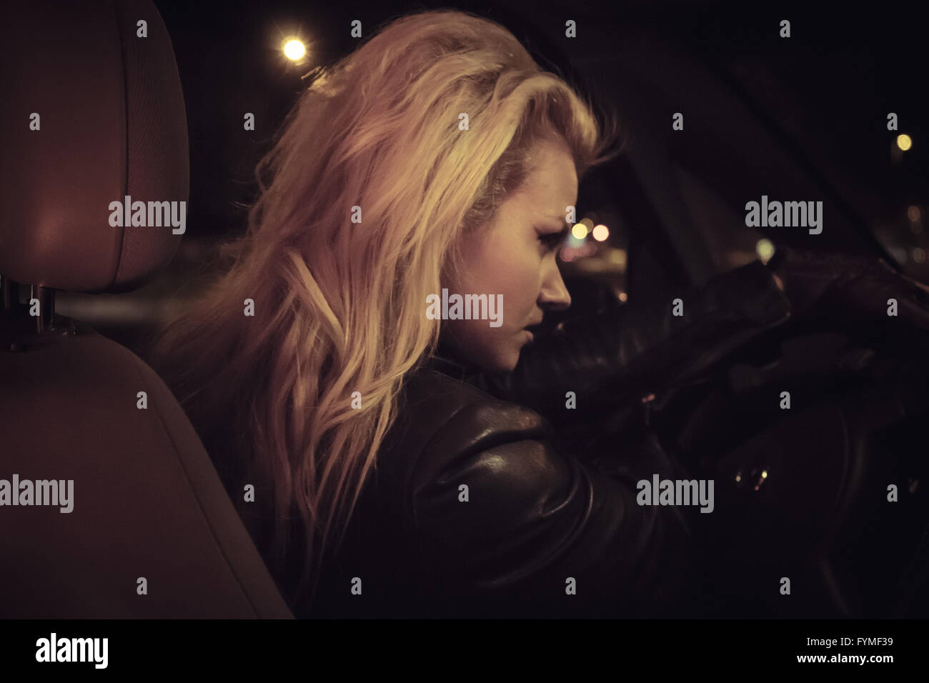 Traffic, aggressive look blonde driving a car at night in the city ...