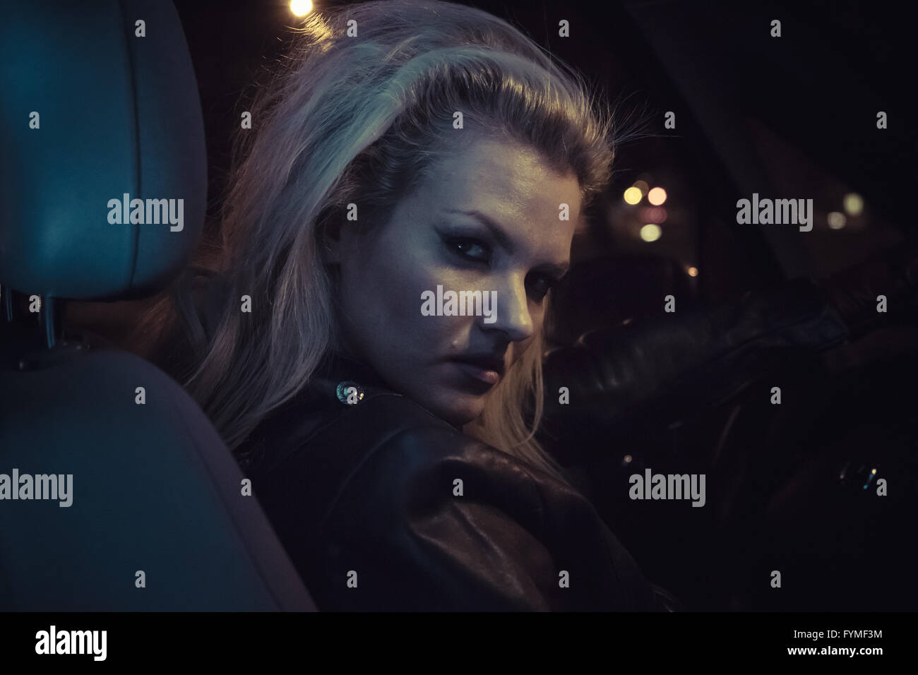 Lifestyle, aggressive look blonde driving a car at night in the city ...