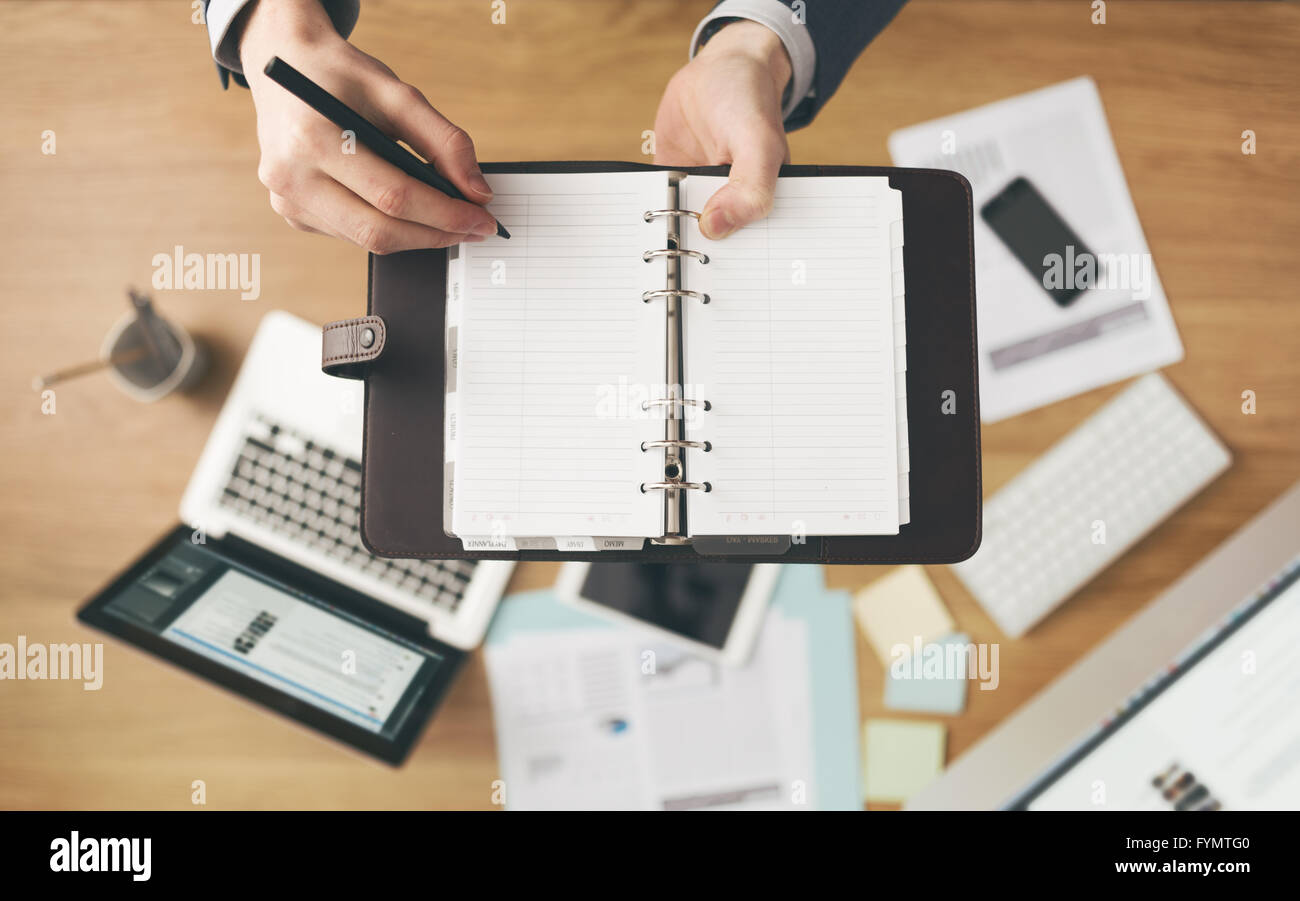 Businessman working at office desk and writing down notes on his agenda ...