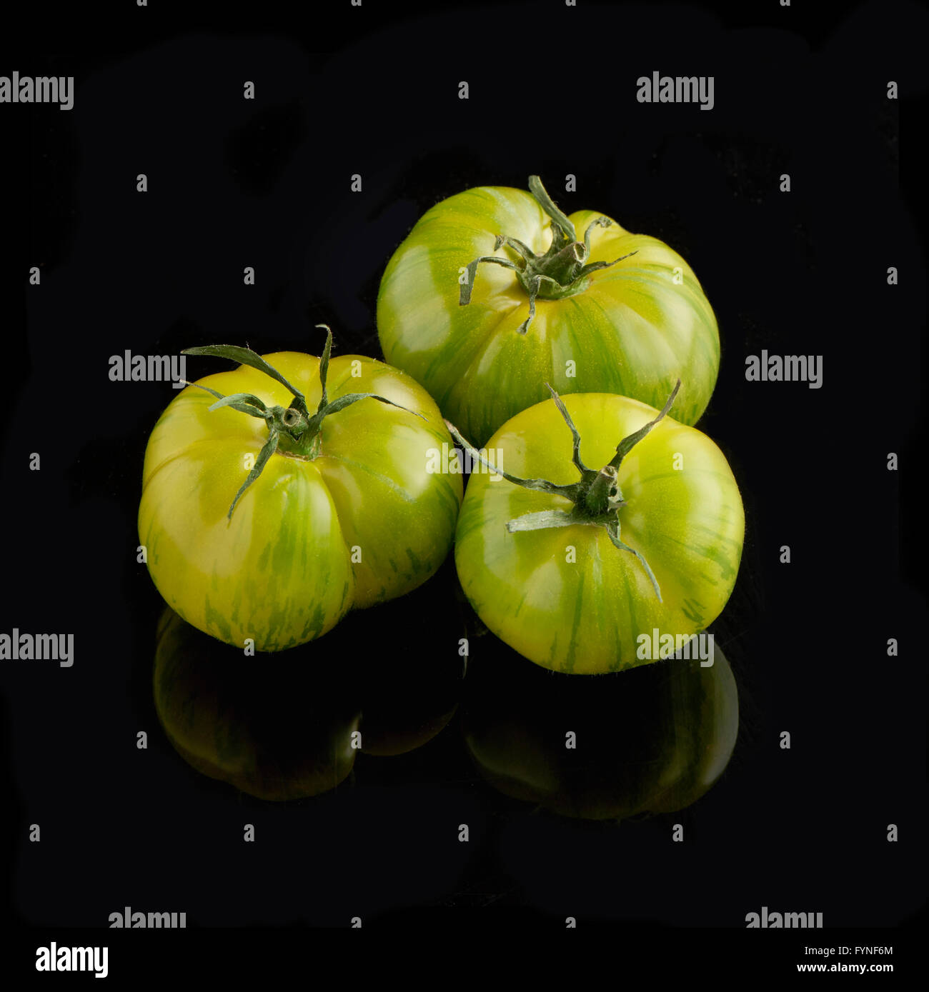 Three fresh whole green tiger tomatoes on a black background with ...