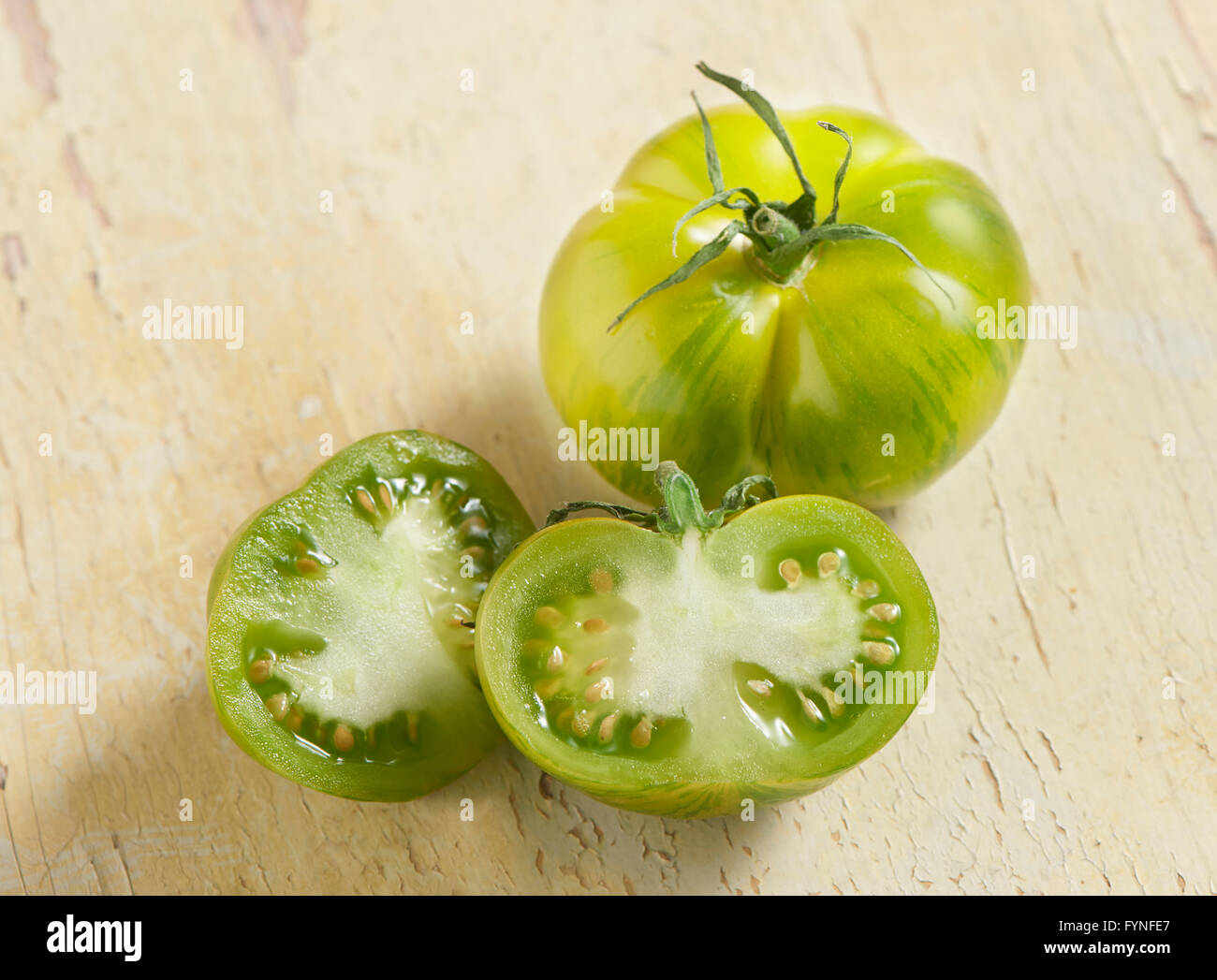 Whole and halved fresh green tiger tomatoes on a wooden background in a ...
