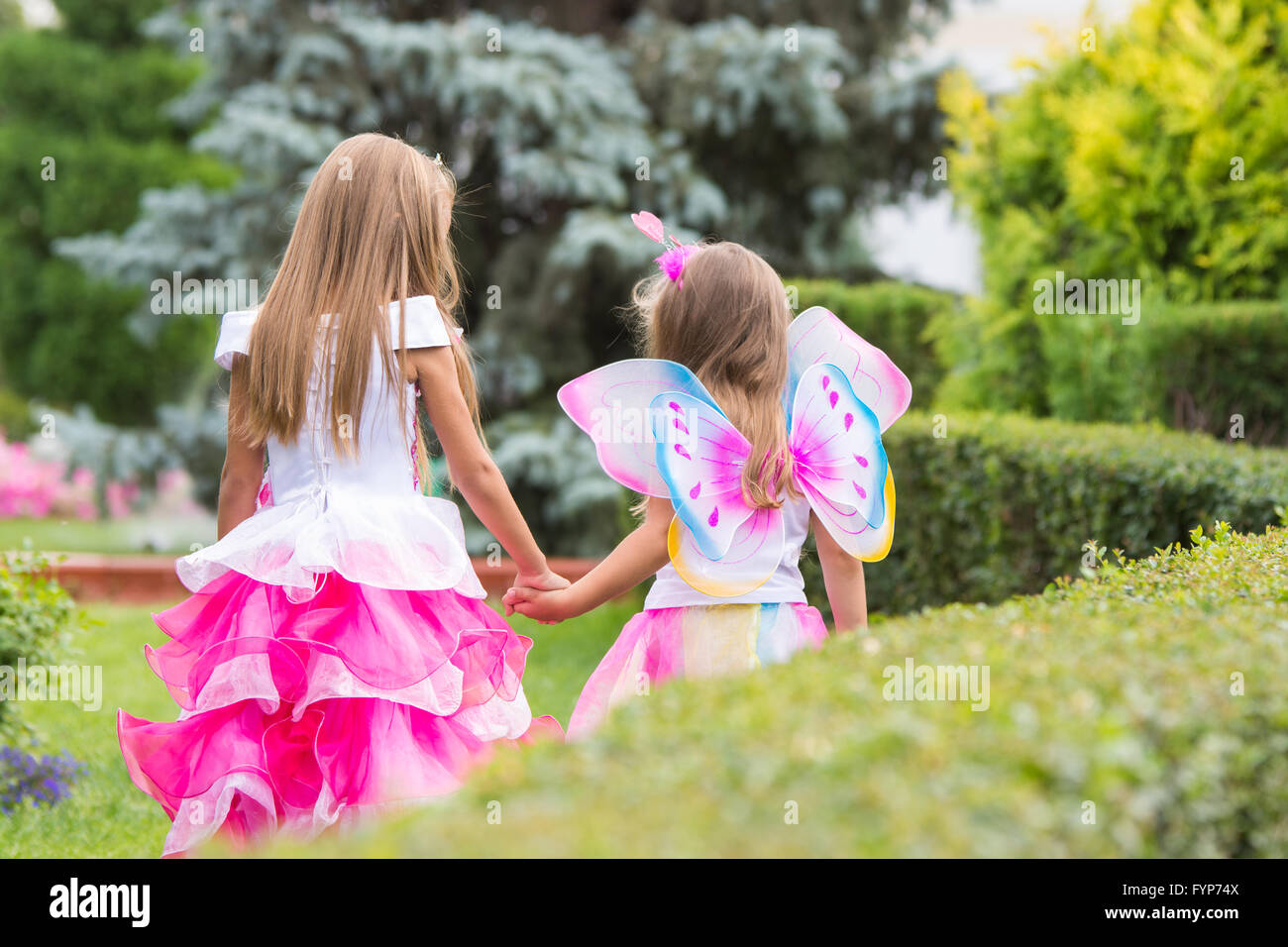 Two little girls, princess and fairy, walk hands in the garden Stock ...