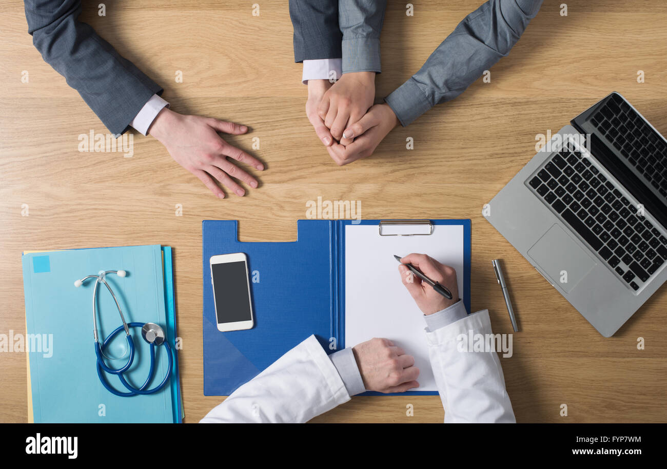 Doctor writing down medical records and talking with a couple during a ...