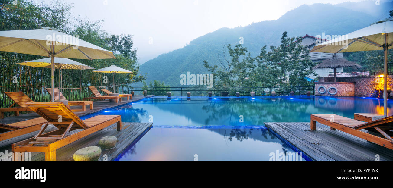 Umbrella chair in hotel pool resort with sunset Stock Photo - Alamy