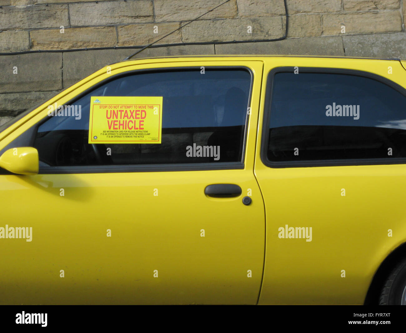 A small yellow car with DVLA Untaxed Vehicle notice in the front window ...