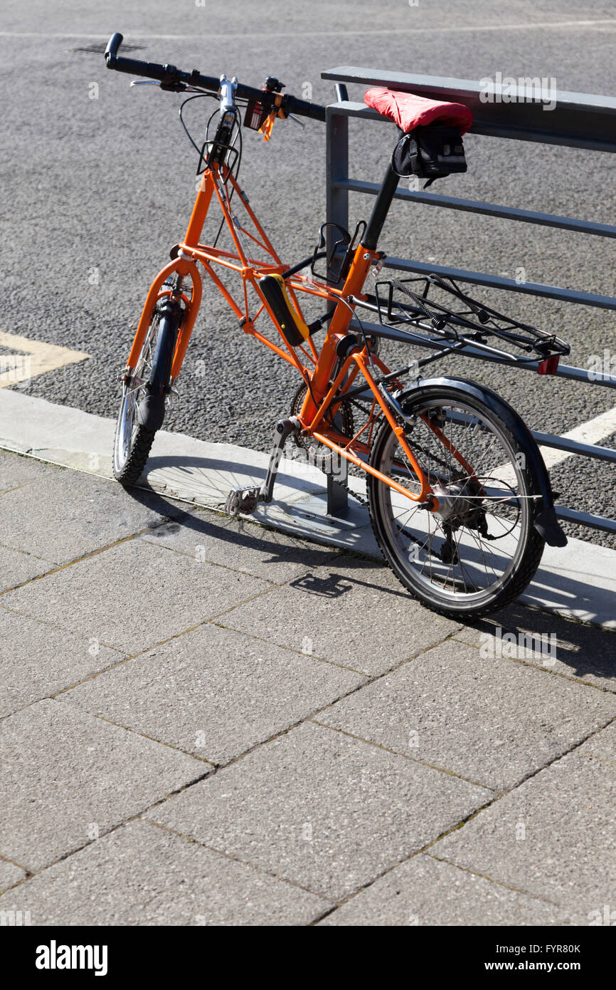 An orange Moulton Space frame small wheel bike locked to a fence in ...