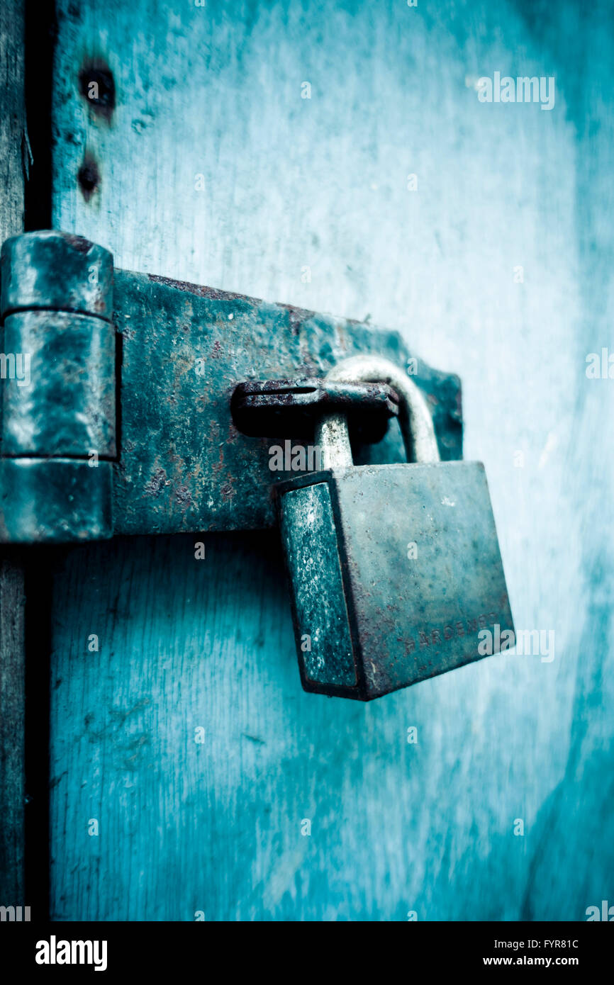 A worn and rusty old padlock on the hasp of a plain and weathered ...