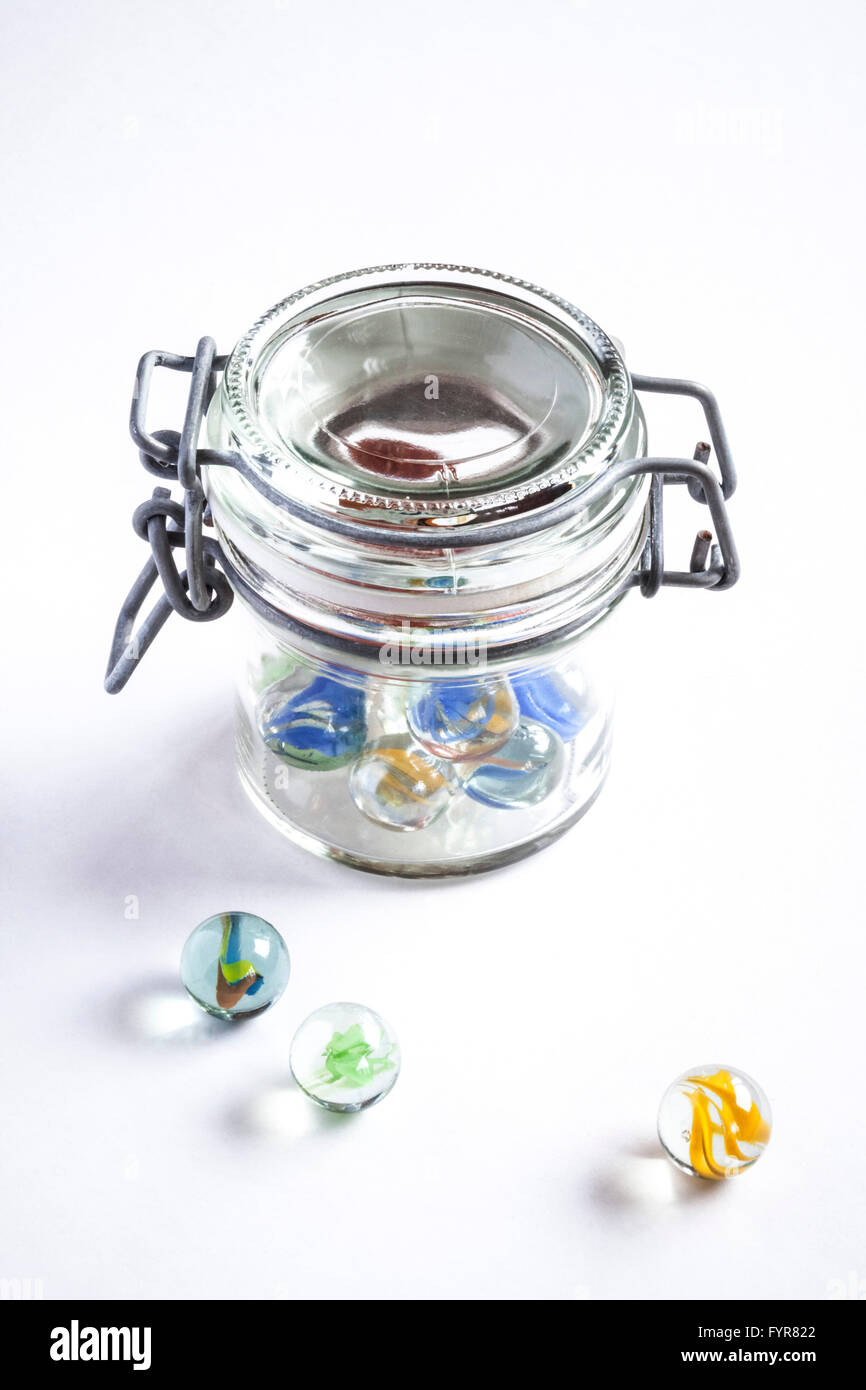A glass jar containing marbles on a white background. Three marbles are ...