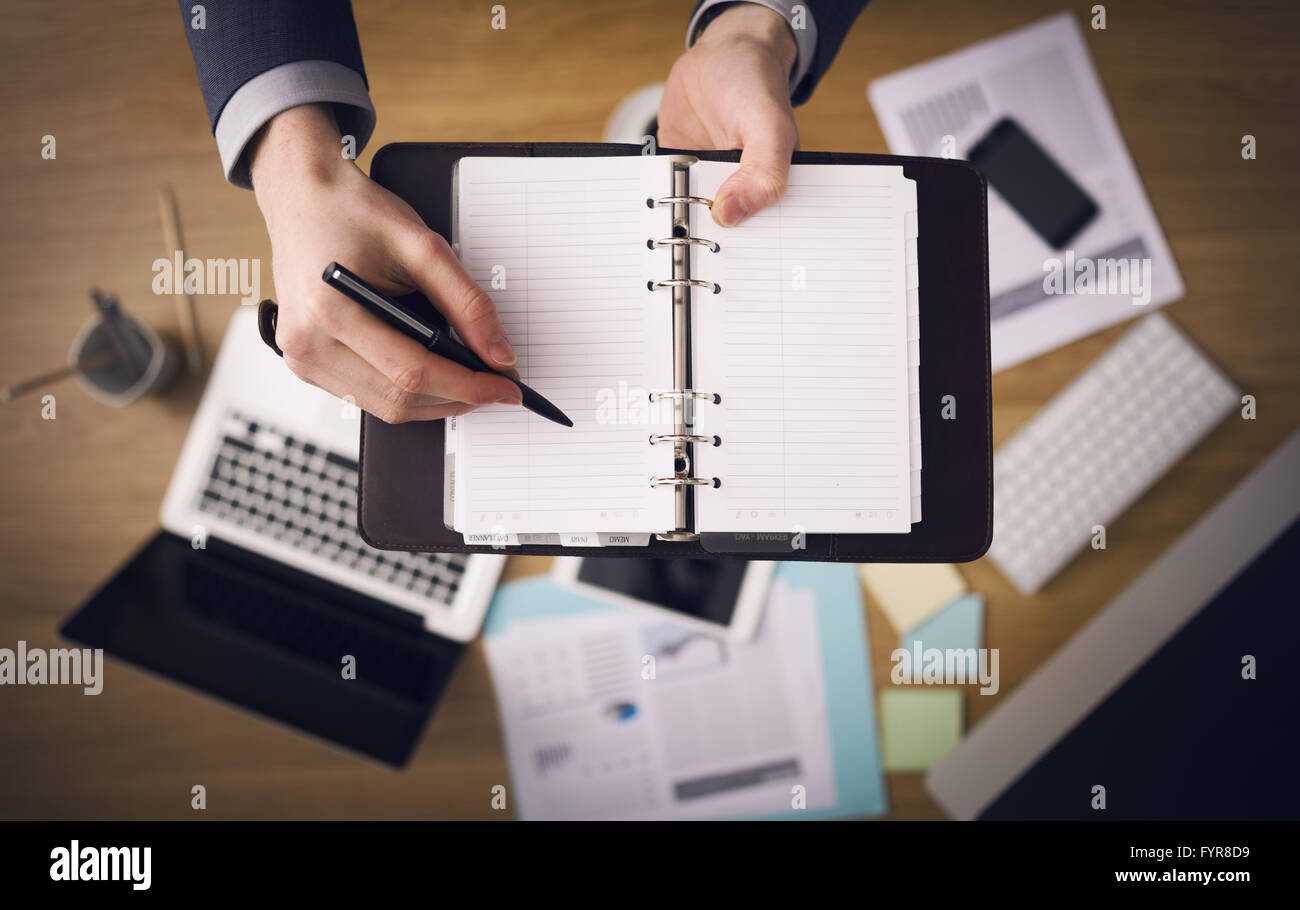 Businessman working at office desk and writing down notes on his agenda ...
