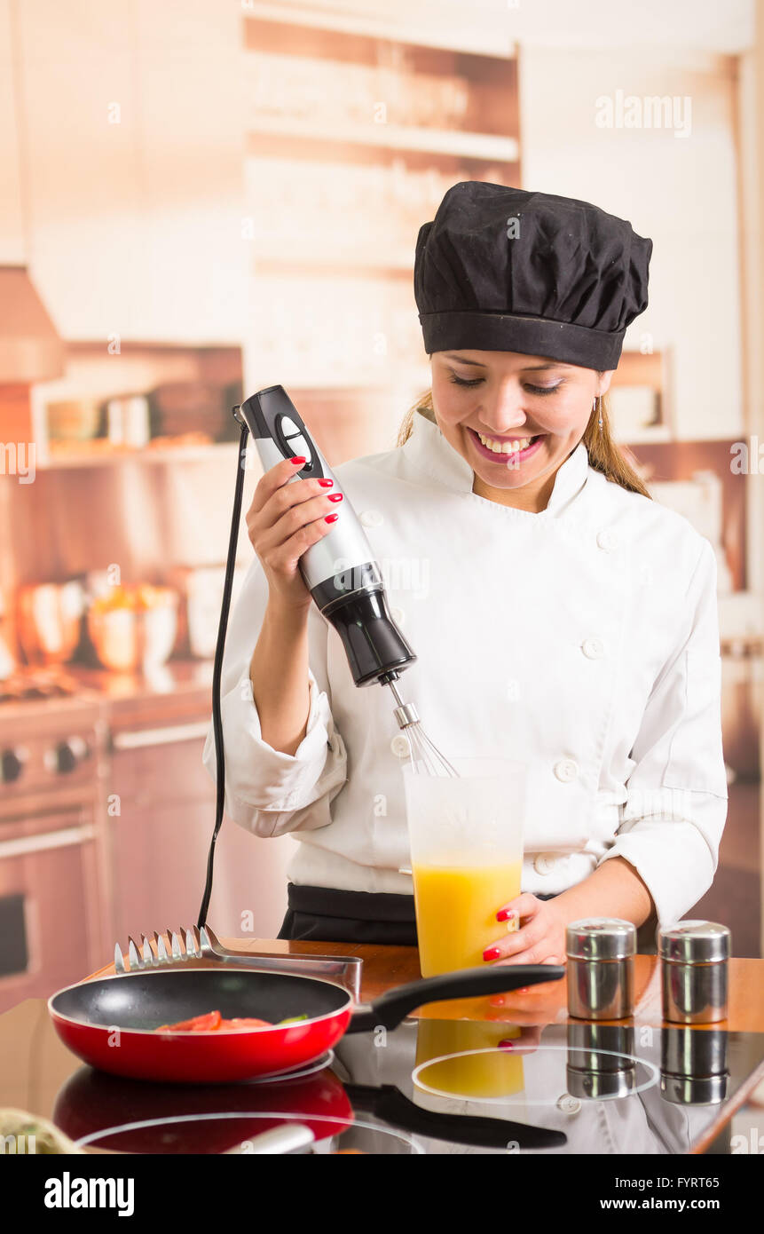 Woman chef wearing full cooking outfit standing using electric blender ...