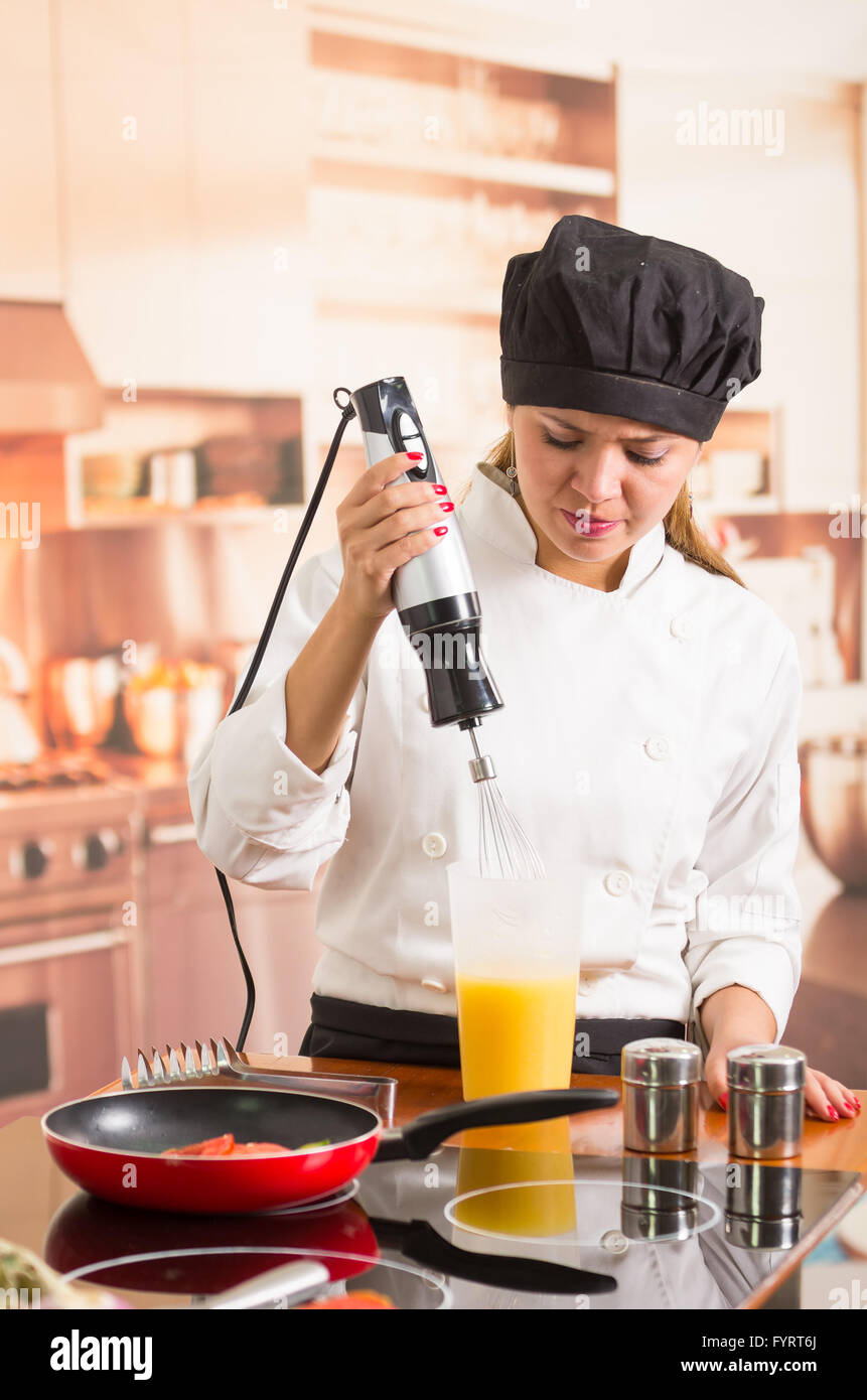 Woman chef wearing full cooking outfit standing using electric blender ...
