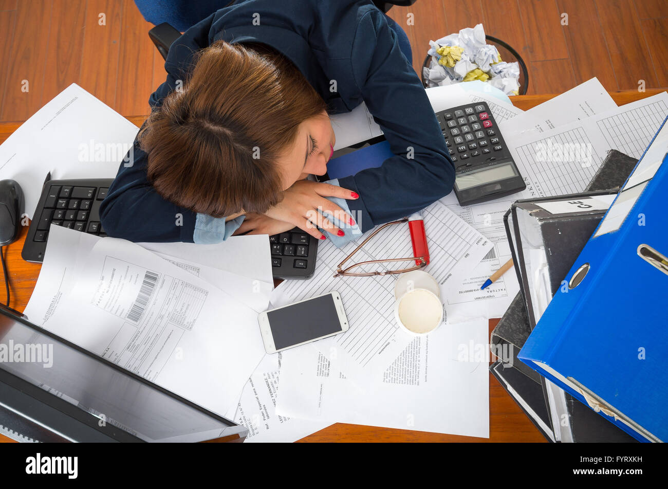 Young woman sitting and lying asleep over office desk with papers ...