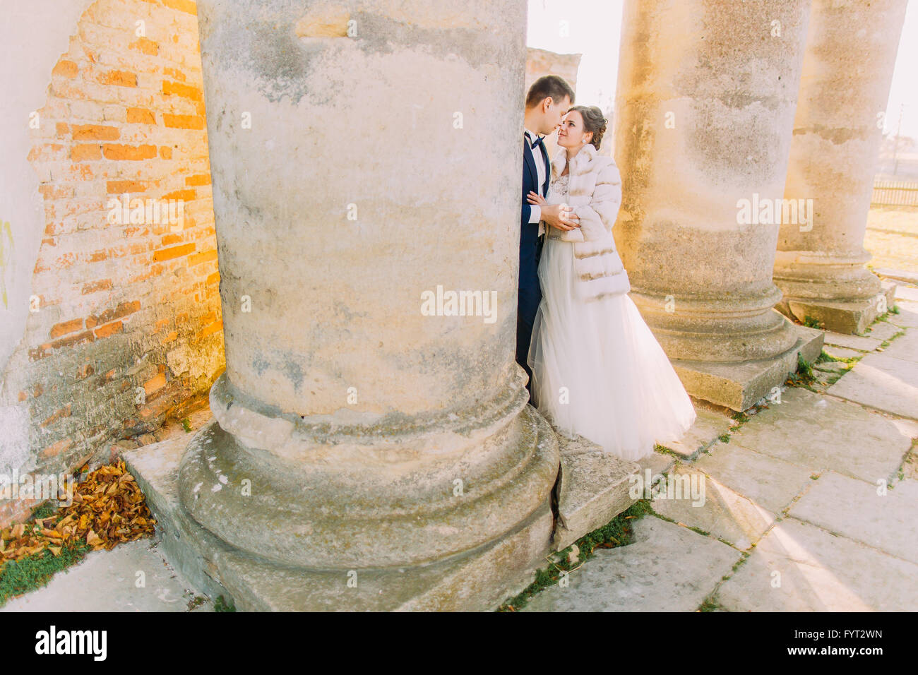 Handsome groom kissing his beautiful bride between two columns at ...