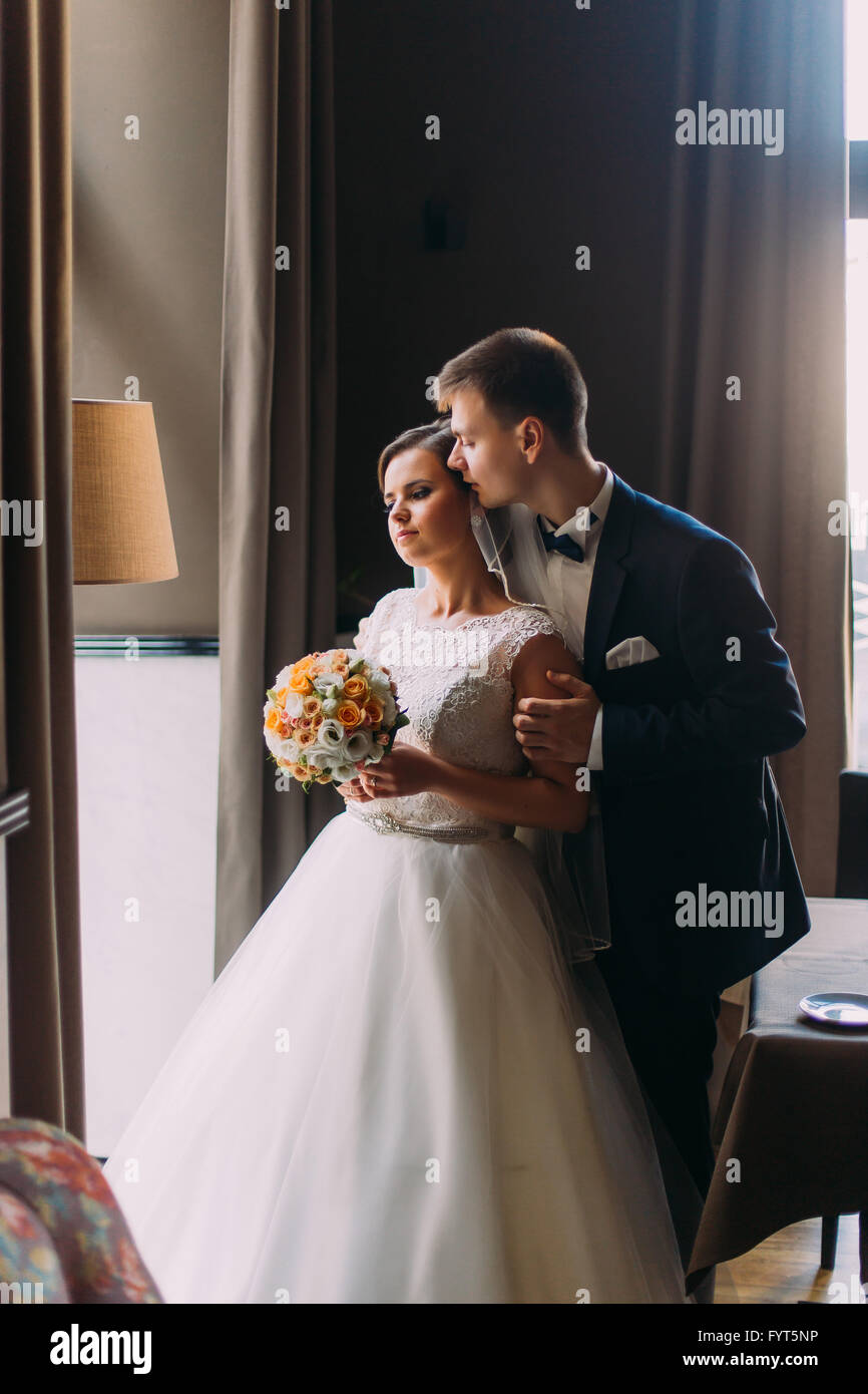 Groom hugging from back bride. Married couple standing by the window ...