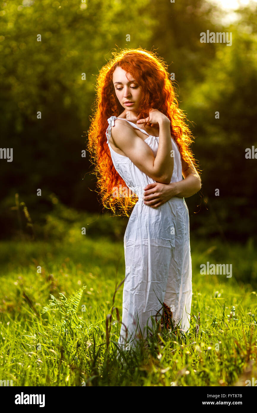 Redhead girl walking under rays of sunset forest Stock Photo - Alamy