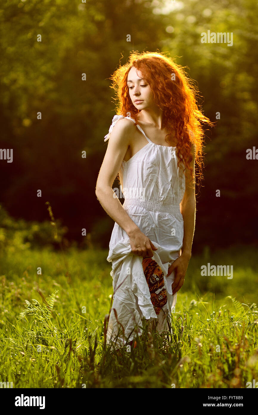 Redhead girl walking under rays of sunset forest Stock Photo - Alamy