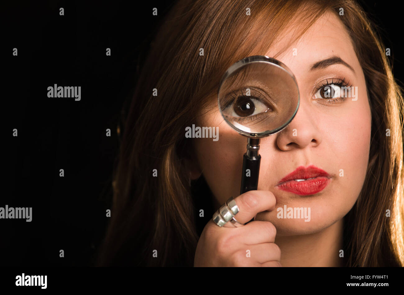 Young woman facing camera holding magnifying glass over right eye ...