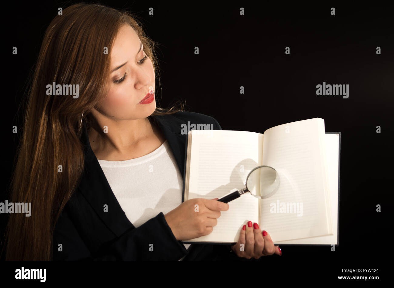 Young brunette woman facing camera holding up open book and magnifying ...