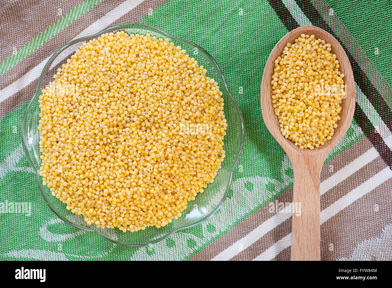 Tiny millet hulled grains lying on glass saucer and wooden spoon on ...