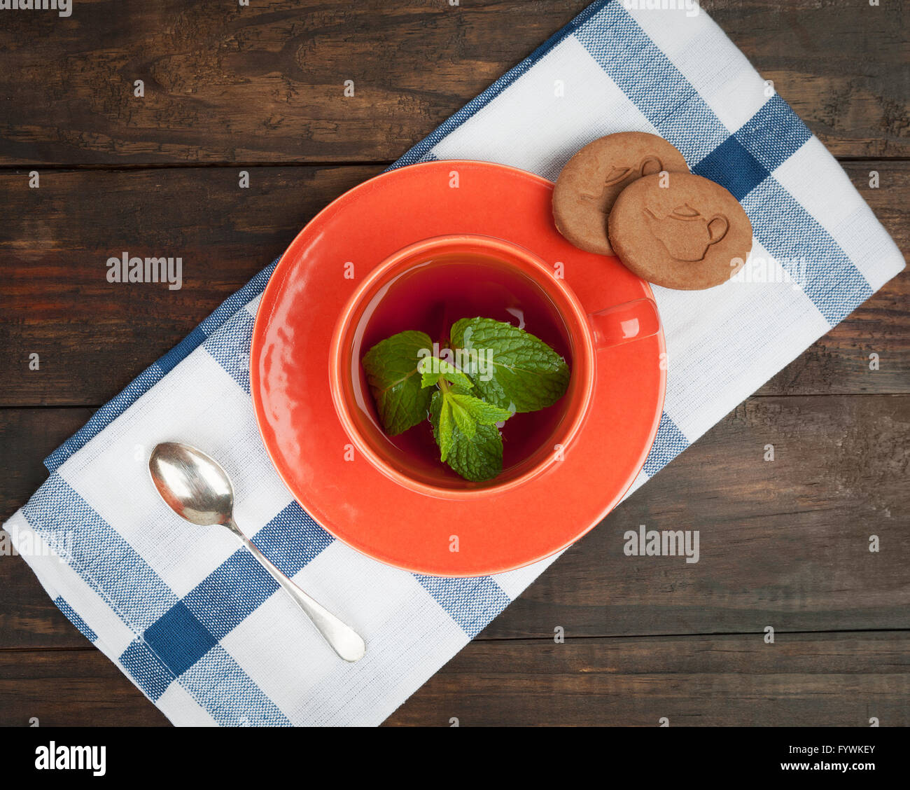 Orange teacup with tea and mint placed on teatowel together with spoon ...