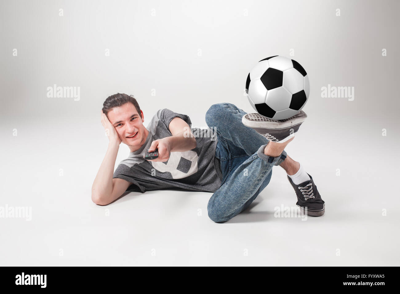The portrait of fan with ball, holding tv remote on gray background ...