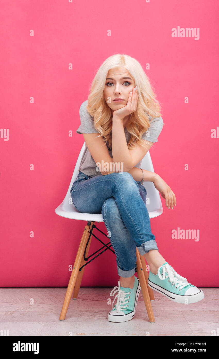 Sad young woman sitting on the chair over pink background Stock Photo ...